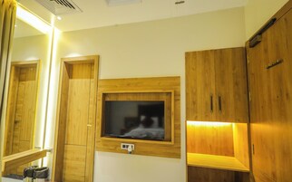 Quarto com armários de madeira, televisão montada na parede e um espelho refletindo parte do ambiente.
