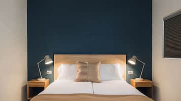 Cama bem arrumada com duas luminárias de cabeceira, cabeceira de madeira e parede escura ao fundo.