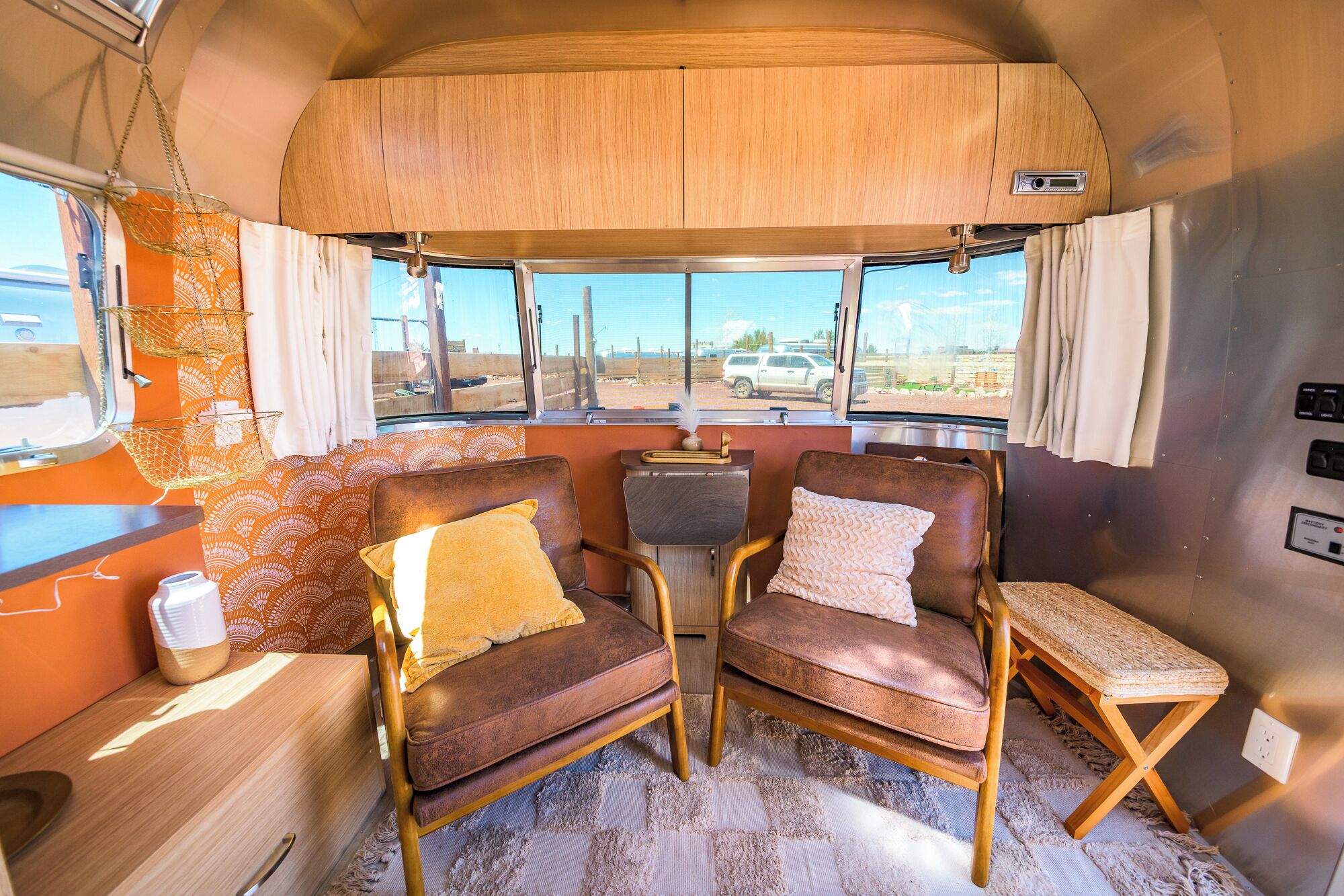 Interior acolhedor de uma van, com duas poltronas de couro, uma mesa pequena e uma janela com vista para o exterior.
