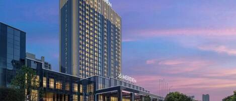 Um hotel moderno com um edifício alto e retangular e um anexo mais baixo com fachada de vidro.