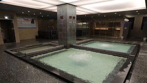 Um saguão de hotel com uma mesa de recepção, um relógio digital e uma grande cascata.
