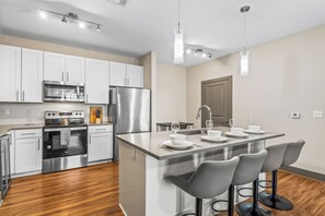 Cozinha moderna com eletrodomésticos de aço inoxidável, uma ilha central com banquetas e uma área de refeições com uma mesa pequena e cadeiras.