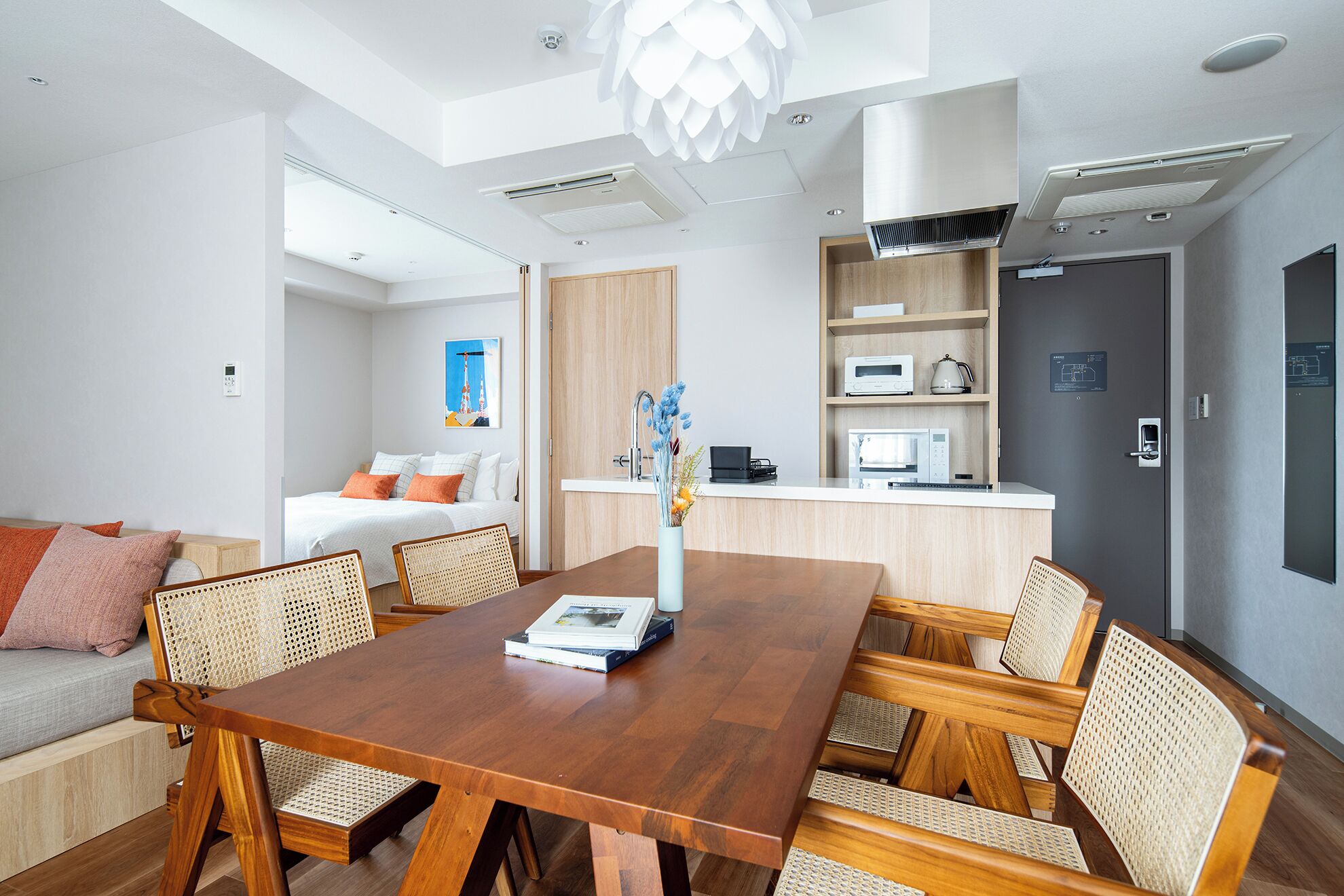 Quarto de hotel moderno com mesa de jantar de madeira, cadeiras de vime, cozinha compacta, cama com vista e uma janela grande.