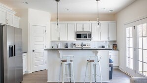 Uma cozinha moderna com armários brancos, eletrodomésticos de aço inoxidável e iluminação pendente.
