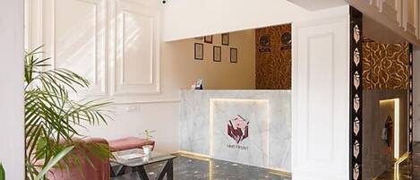 Uma área de recepção com balcão de mármore, quadros nas paredes e um vaso de planta.