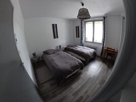 Quarto com cama grande, mesa pequena, cadeira e janela com cortinas.