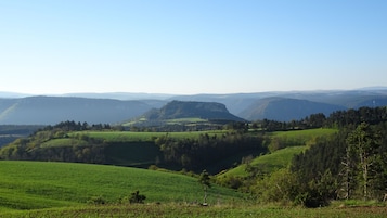 Vista panorâmica de colinas verdes ondulantes e montanhas distantes sob um céu claro.