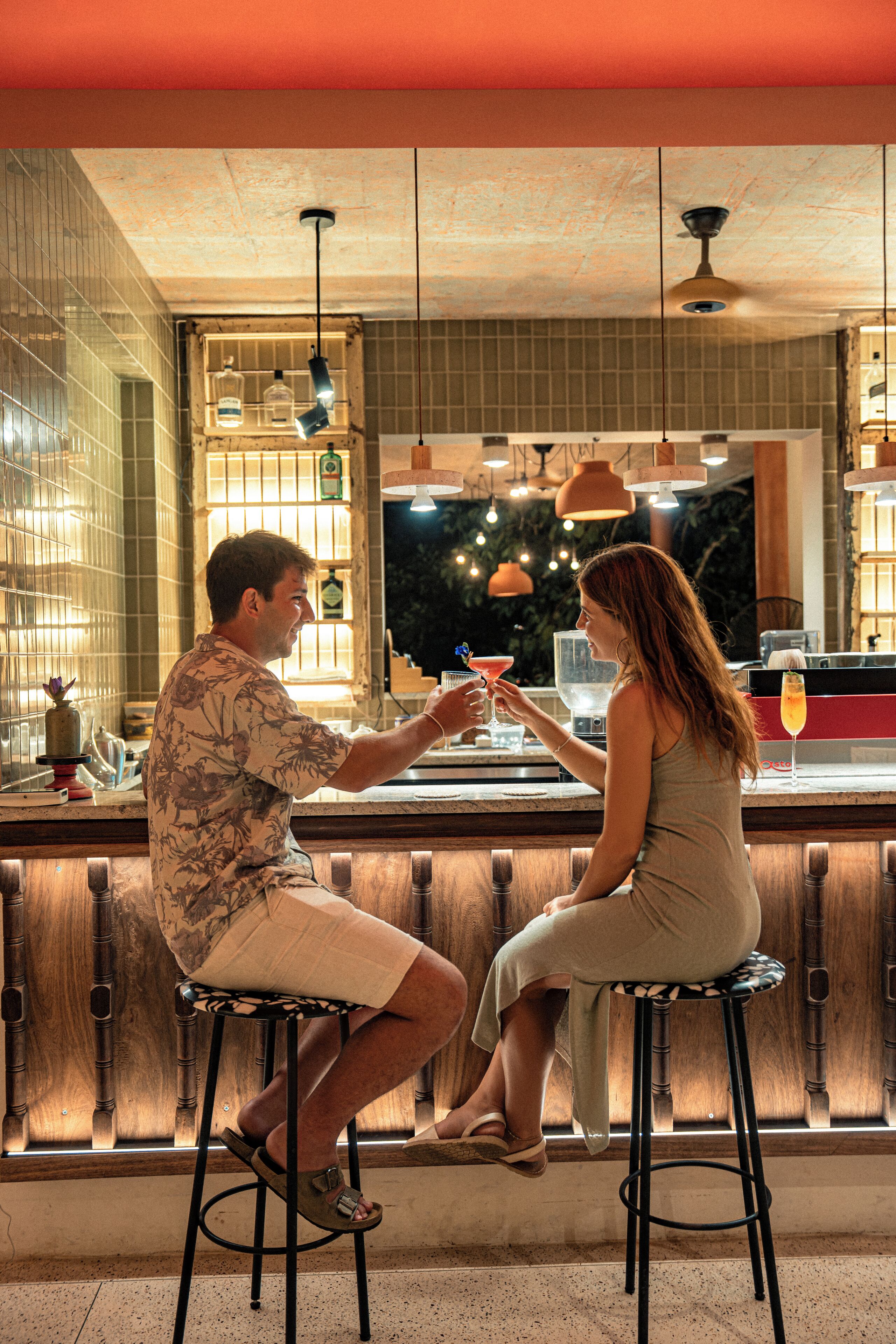Uma área de bar com dois bancos, uma pessoa segurando uma bebida e outra sentada.