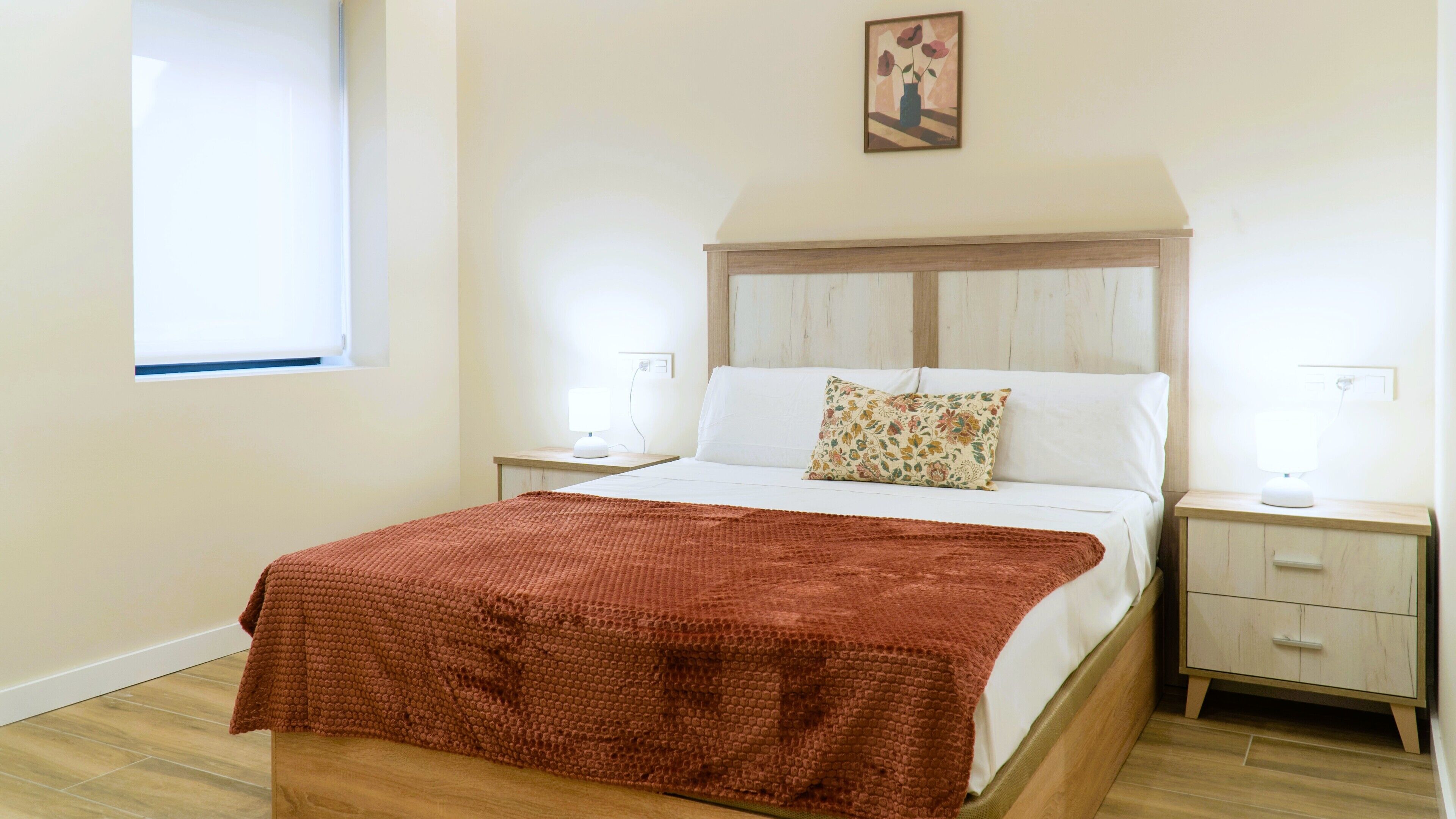 Quarto bem arrumado com cama, mesa de cabeceira, abajur e janela.