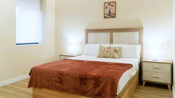 Quarto bem arrumado com cama, mesa de cabeceira, abajur e janela.