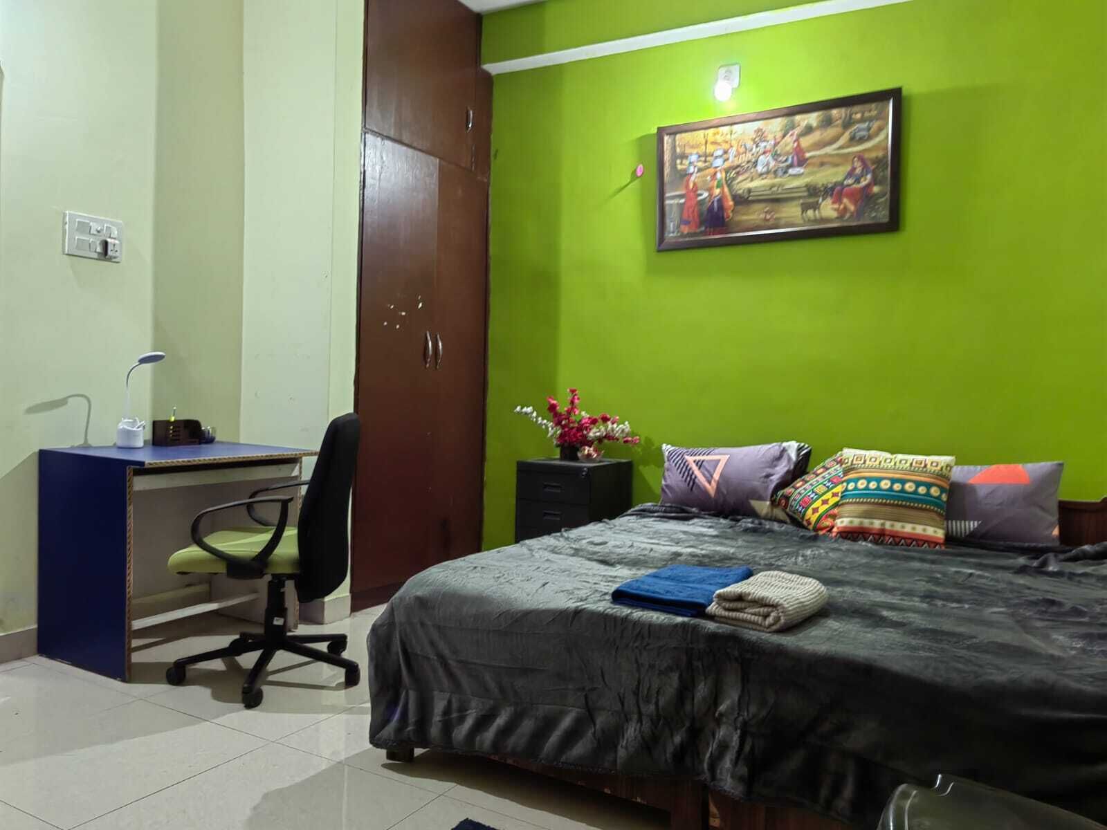 Quarto com cama, escrivaninha, cadeira e parede verde com pintura.