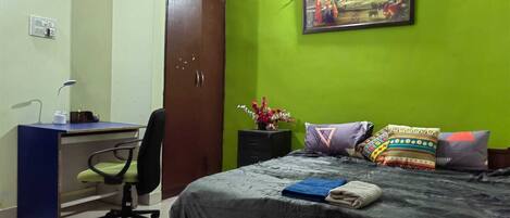 Quarto com cama, escrivaninha, cadeira e parede verde com pintura.