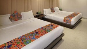 Quarto de hotel com duas camas, cada uma com um cobre-leito colorido, um ventilador de teto e iluminação embutida.