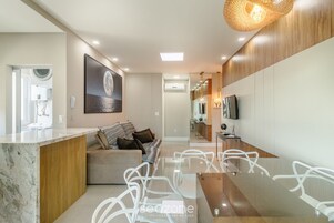 Uma sala de estar moderna com uma ilha de mármore, um sofá com almofadas, uma mesa de jantar com cadeiras e um quadro grande na parede.