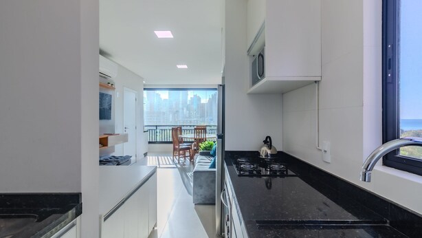 Uma cozinha moderna com bancada preta, pia de aço inoxidável e janela com vista para a paisagem urbana.