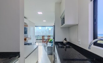 Uma cozinha moderna com bancada preta, pia de aço inoxidável e janela com vista para a paisagem urbana.