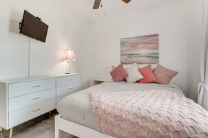 Quarto com cama, mesa de cabeceira com abajur, televisão na parede e um quadro sobre a cama.