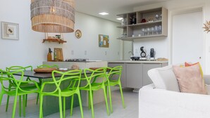 Cozinha moderna com área de jantar, cadeiras verdes, sofá branco e luminária pendente.