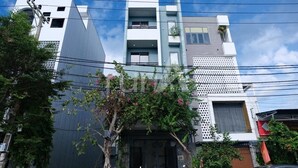 Um edifício moderno de vários andares, com um telhado triangular marcante, varandas e uma entrada com portão.