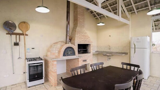 Uma cozinha com forno de tijolos, fogão a gás, geladeira e mesa de jantar com cadeiras.