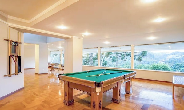 Uma mesa de bilhar em um espaço com janelas amplas e vista para o exterior.