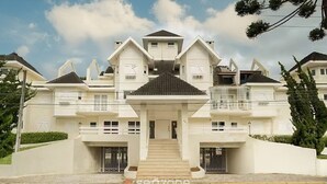 Uma casa grande e moderna com dois andares e design simétrico, apresentando uma escadaria central, várias varandas e um jardim da frente bem cuidado.