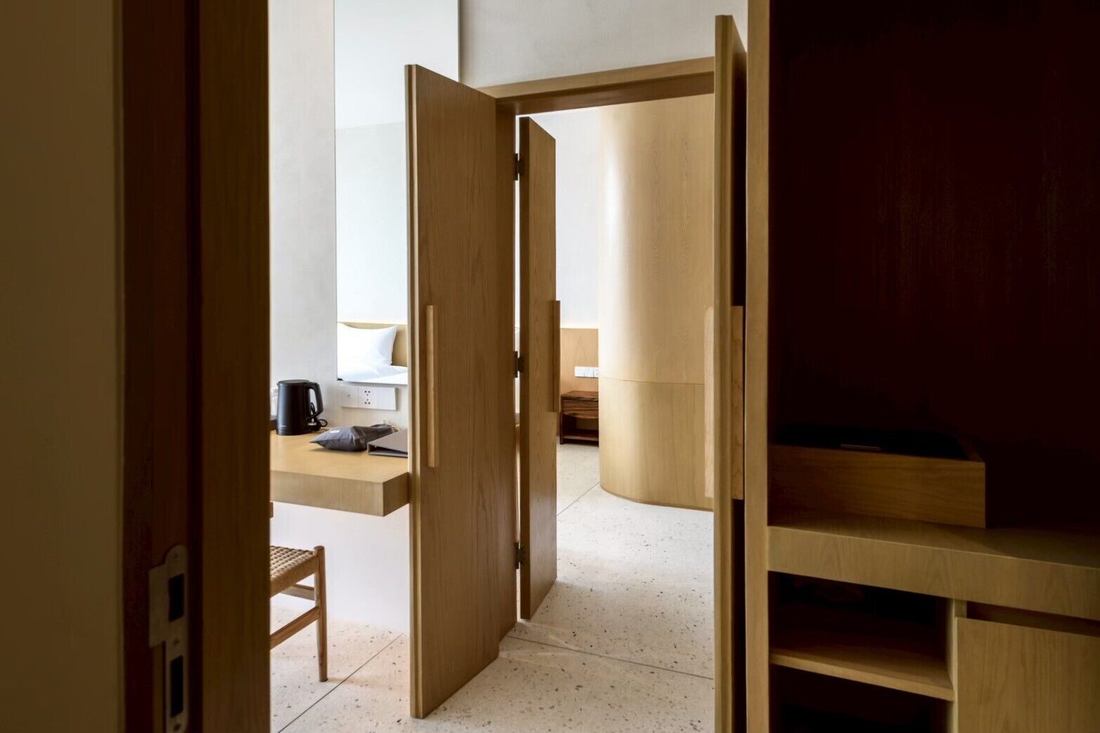 Quarto de hotel moderno com uma escrivaninha de madeira, uma cama e um grande colunar cilíndrico.