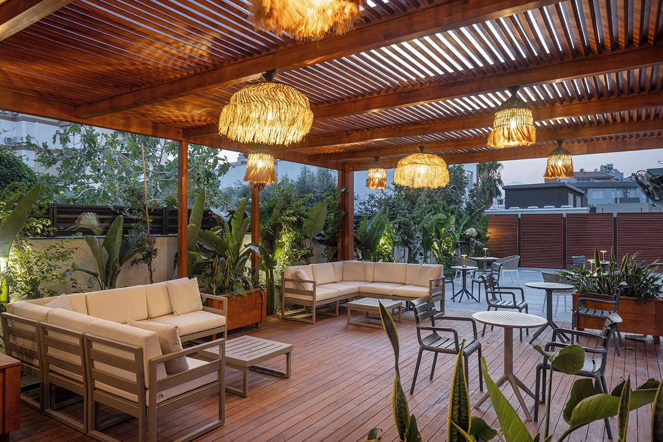 Um terraço ao ar livre com piso de madeira, um sofá, cadeiras e luminárias pendentes.