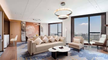 Quarto de hotel moderno com um sofá grande, uma mesa de centro e vista para a cidade.