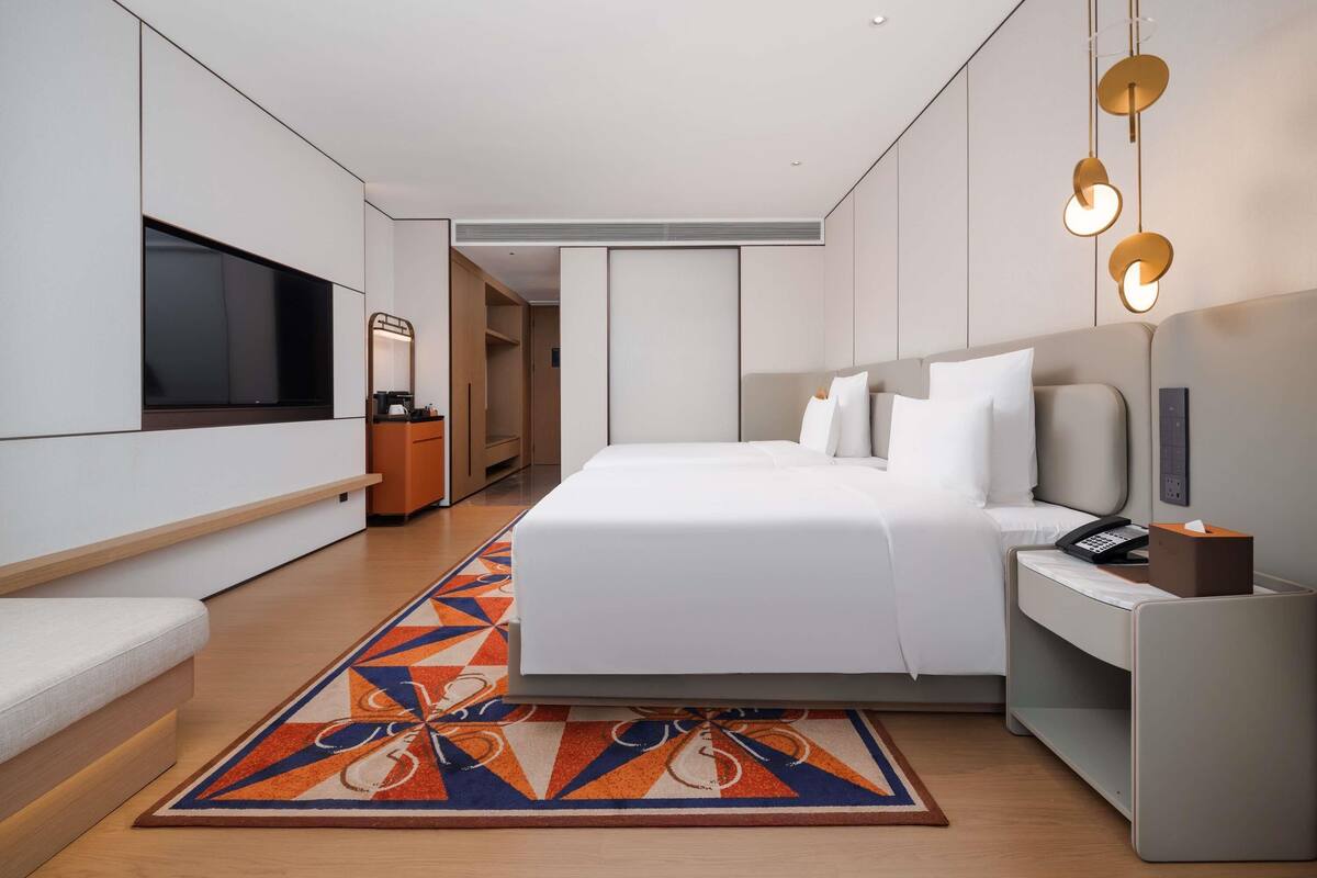 Quarto de hotel moderno com uma cama grande, TV, escrivaninha e closet espaçoso.