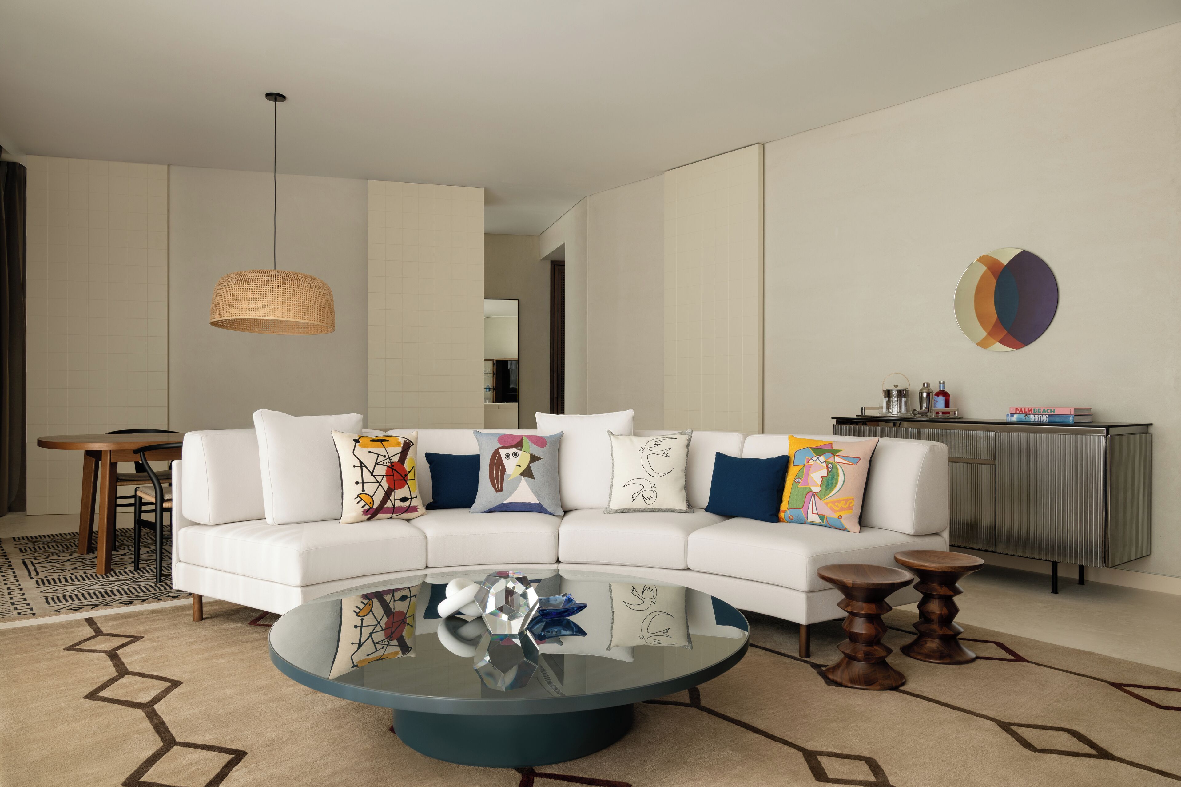 Uma sala de estar moderna com um sofá branco em formato de L, uma mesa de centro de vidro e uma luminária pendente.
