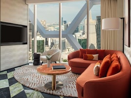 Sala de estar moderna com sofá, mesa de centro redonda e poltrona, com vista para a cidade através de grandes janelas.
