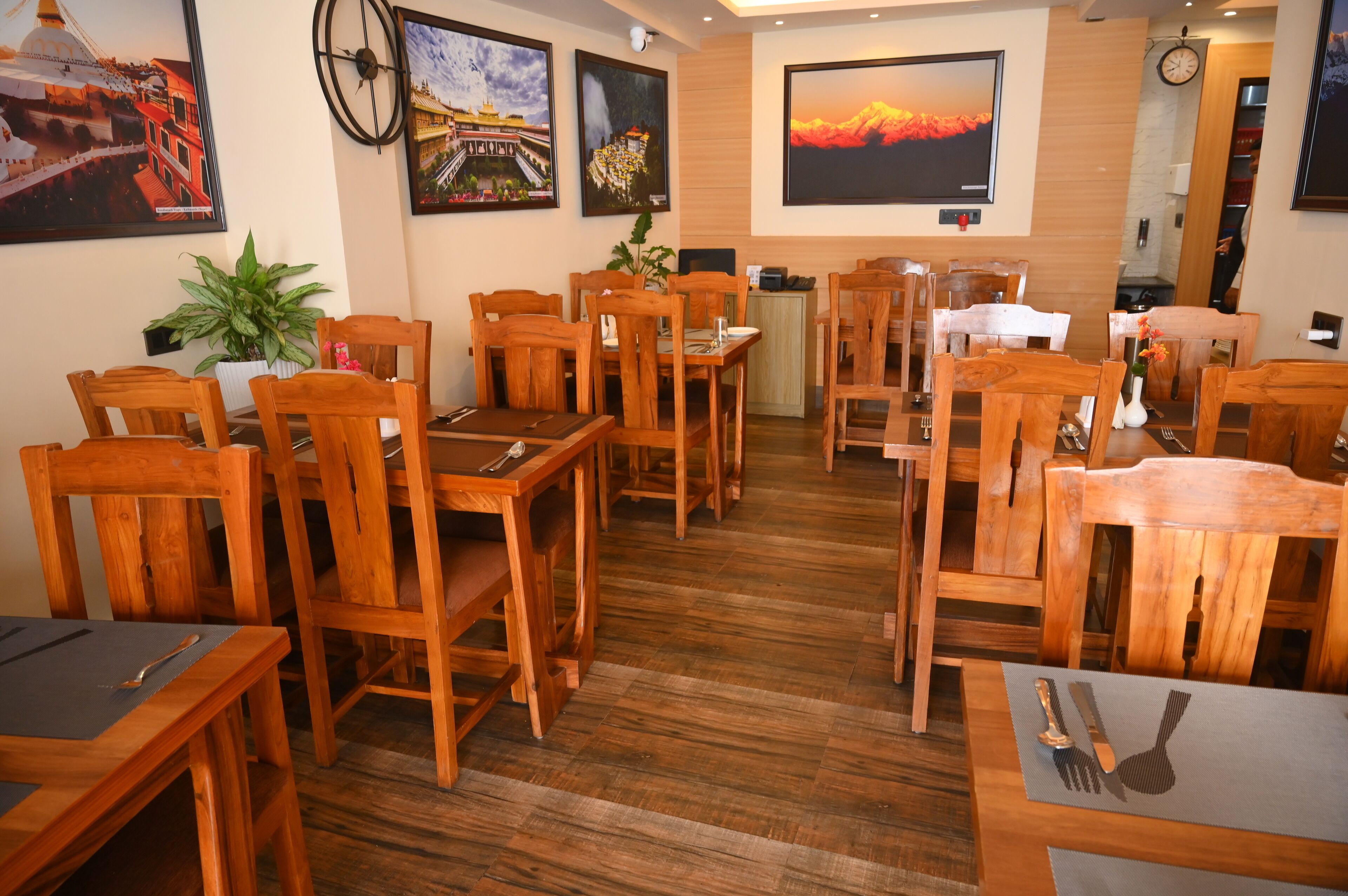 Restaurante com mesas e cadeiras de madeira, um relógio na parede e quadros com imagens de pontos turísticos.