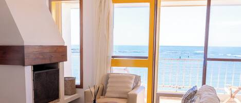 Uma sala de estar moderna com lareira, janelas amplas e vista para o mar.