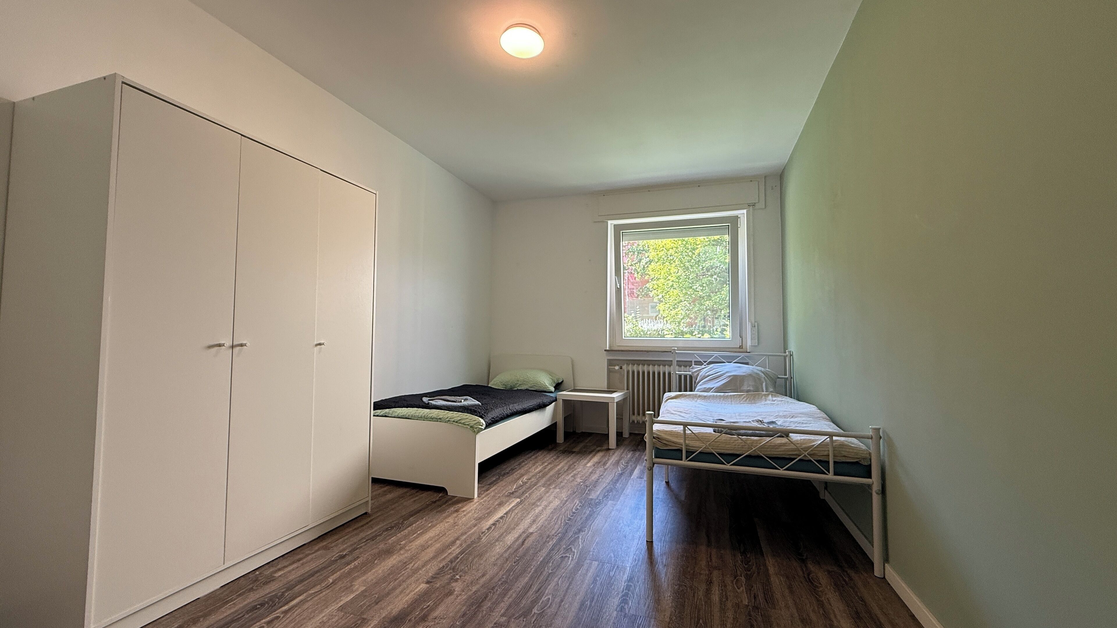 Um apartamento pequeno, de um único quarto, com um guarda-roupa grande, uma janela com vista para o verde e um radiador.