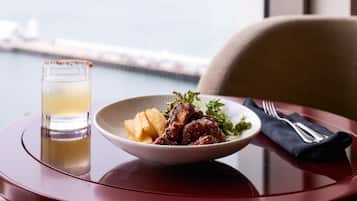 Uma mesa de jantar com um prato de comida, um copo de bebida e vista para um cais.