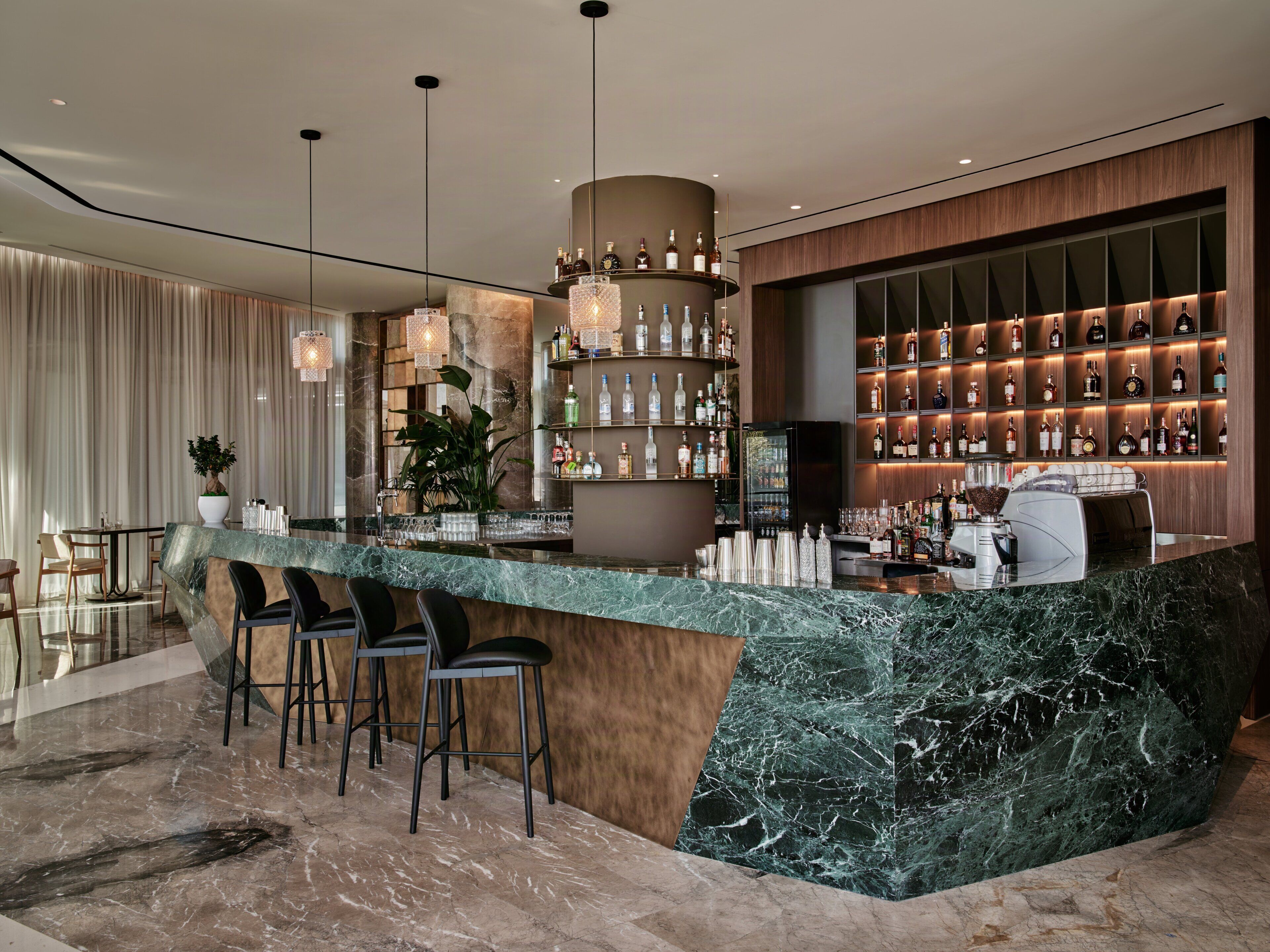 Uma área de bar com bancada de mármore, banquetas, uma grande adega e uma máquina de café.