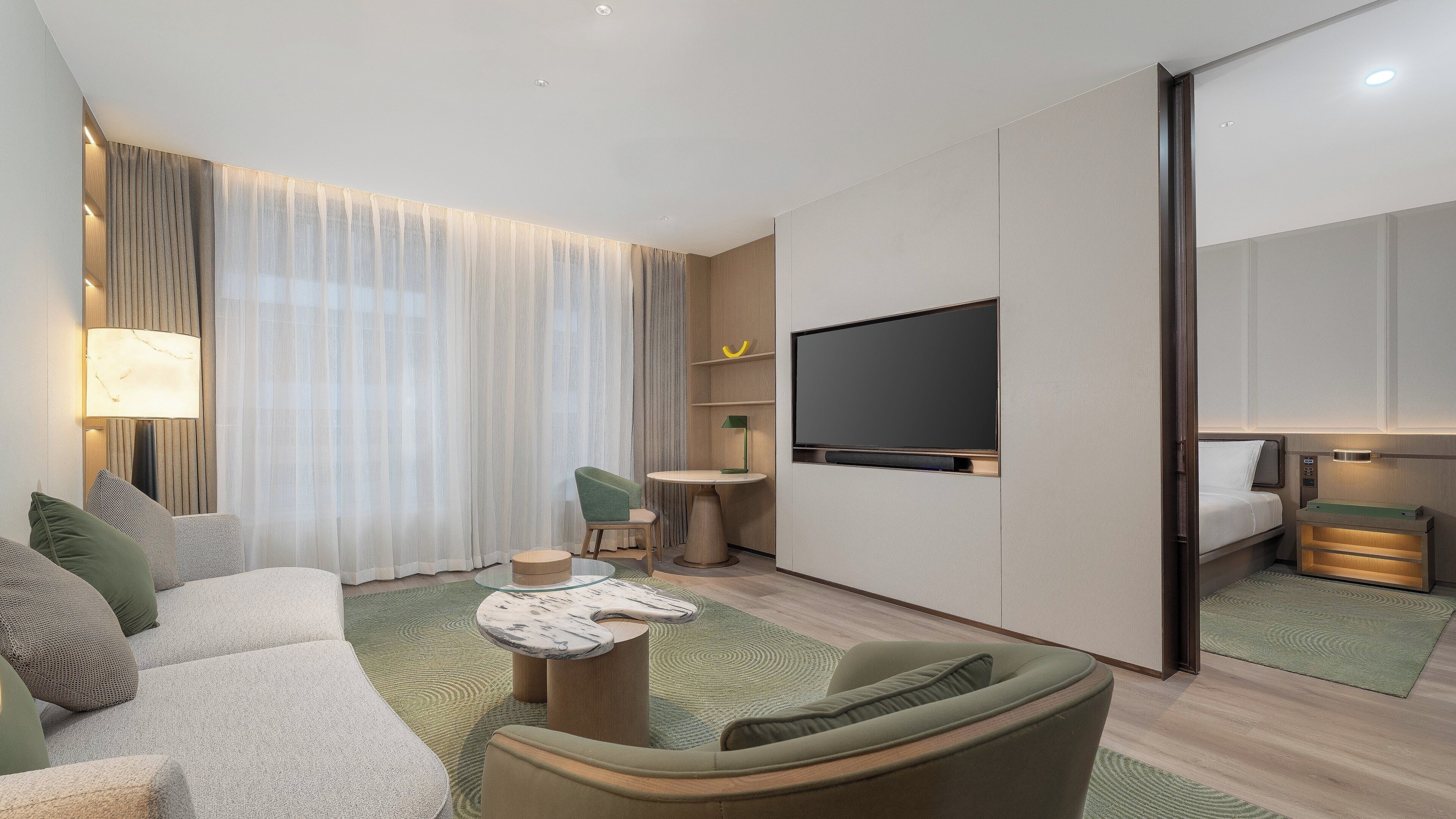 Quarto de hotel moderno com sofá, uma pequena mesa, televisão e espelho.