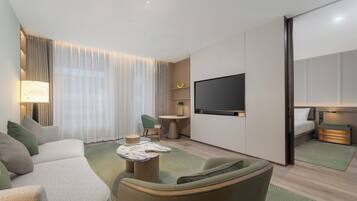 Quarto de hotel moderno com sofá, uma pequena mesa, televisão e espelho.