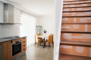 Cozinha moderna com forno embutido, mesa de jantar com cadeiras e escada com padrão geométrico.
