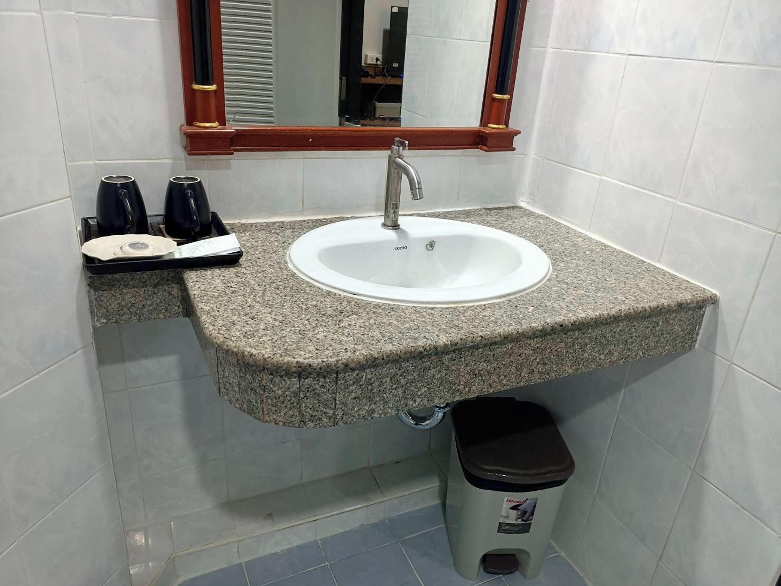 Casa de banho com lavatório de bancada em granito, espelho e lixeira.