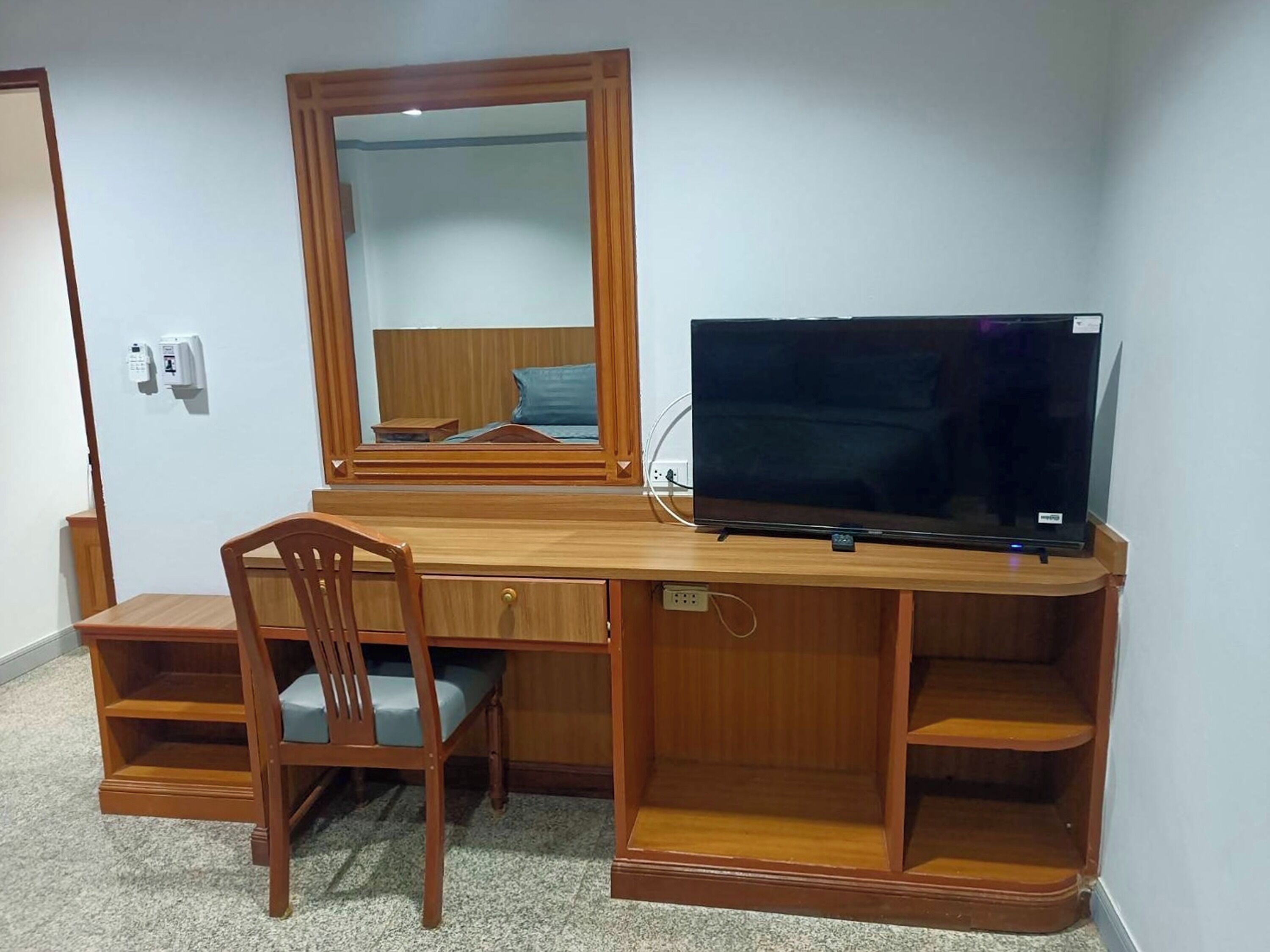 Quarto compacto com escrivaninha de madeira, televisão, cadeira e espelho.