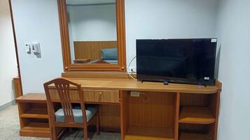 Quarto compacto com escrivaninha de madeira, televisão, cadeira e espelho.