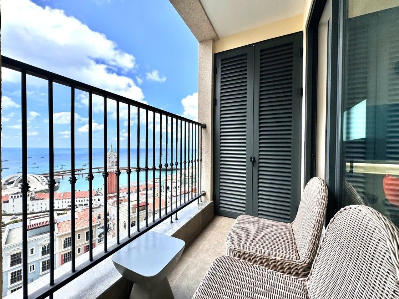 Uma varanda com vista para o mar, uma cadeira de vime e uma mesa pequena.