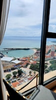 Vista da janela sobre uma área costeira com uma ponte, praia e edifícios.