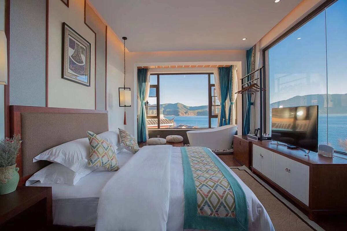 Quarto de hotel com uma cama grande, uma banheira, uma televisão e vista para o mar.