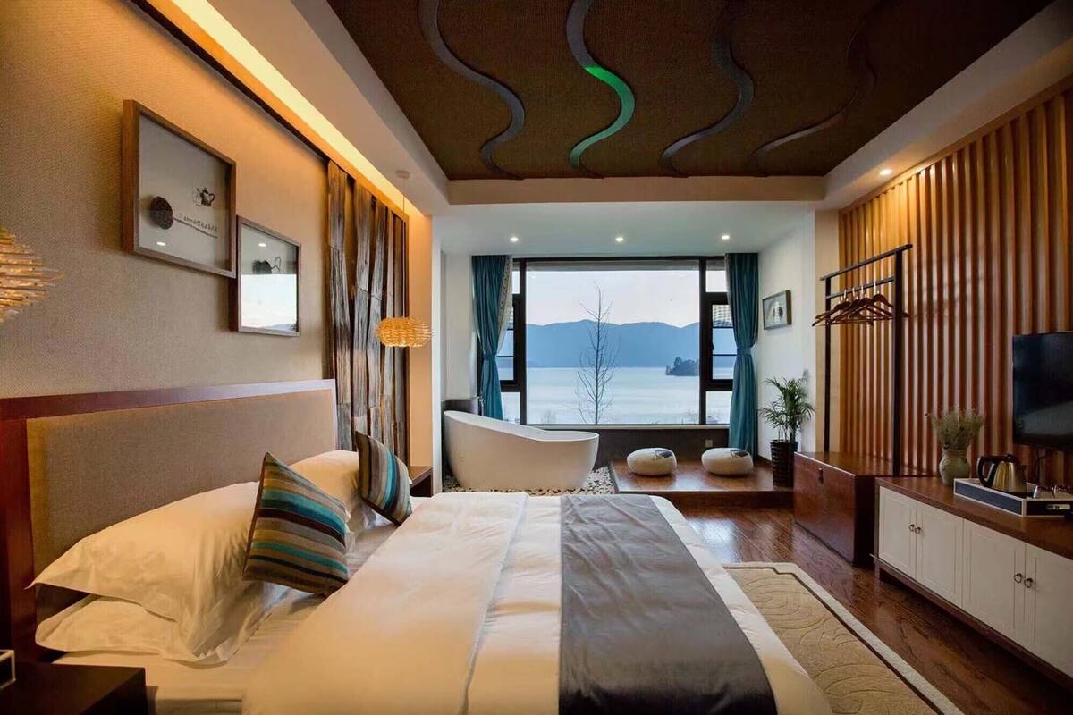 Quarto de hotel moderno com uma cama grande, vista para um lago e uma televisão.