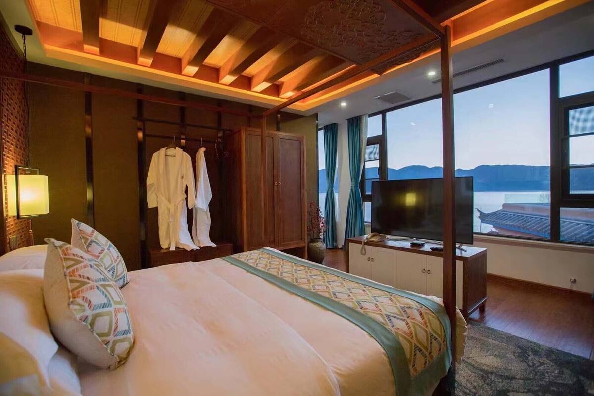 Quarto de hotel com uma cama grande, televisão e vista para as montanhas.