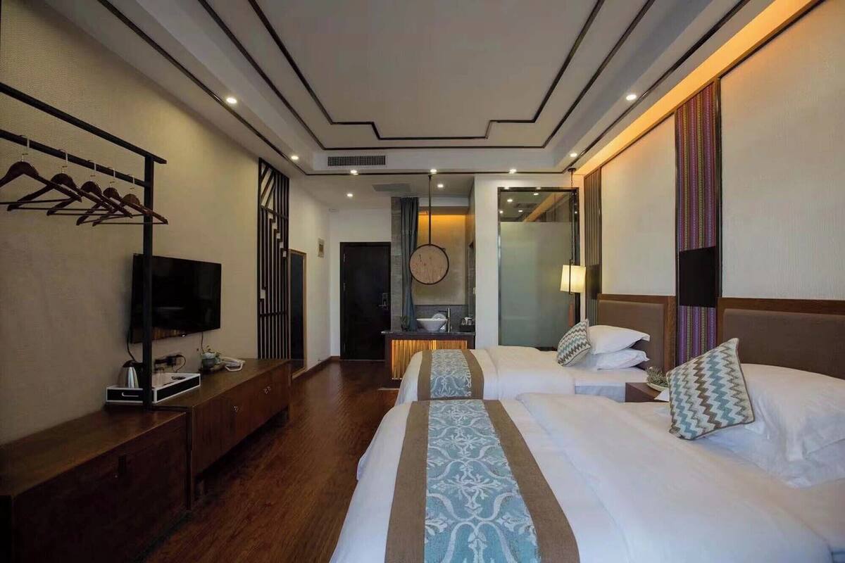 Quarto de hotel com duas camas, uma televisão, uma escrivaninha e um espelho.