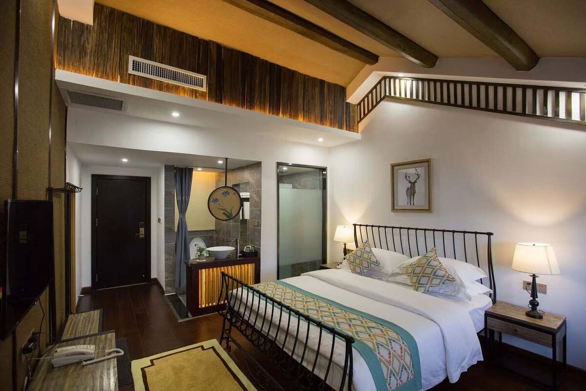 Quarto com uma cama grande, mesa de cabeceira, espelho e porta para um banheiro.